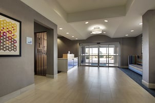 Um saguão de hotel com balcão de recepção, área de espera com sofá e uma grande porta de vidro que dá para o exterior.