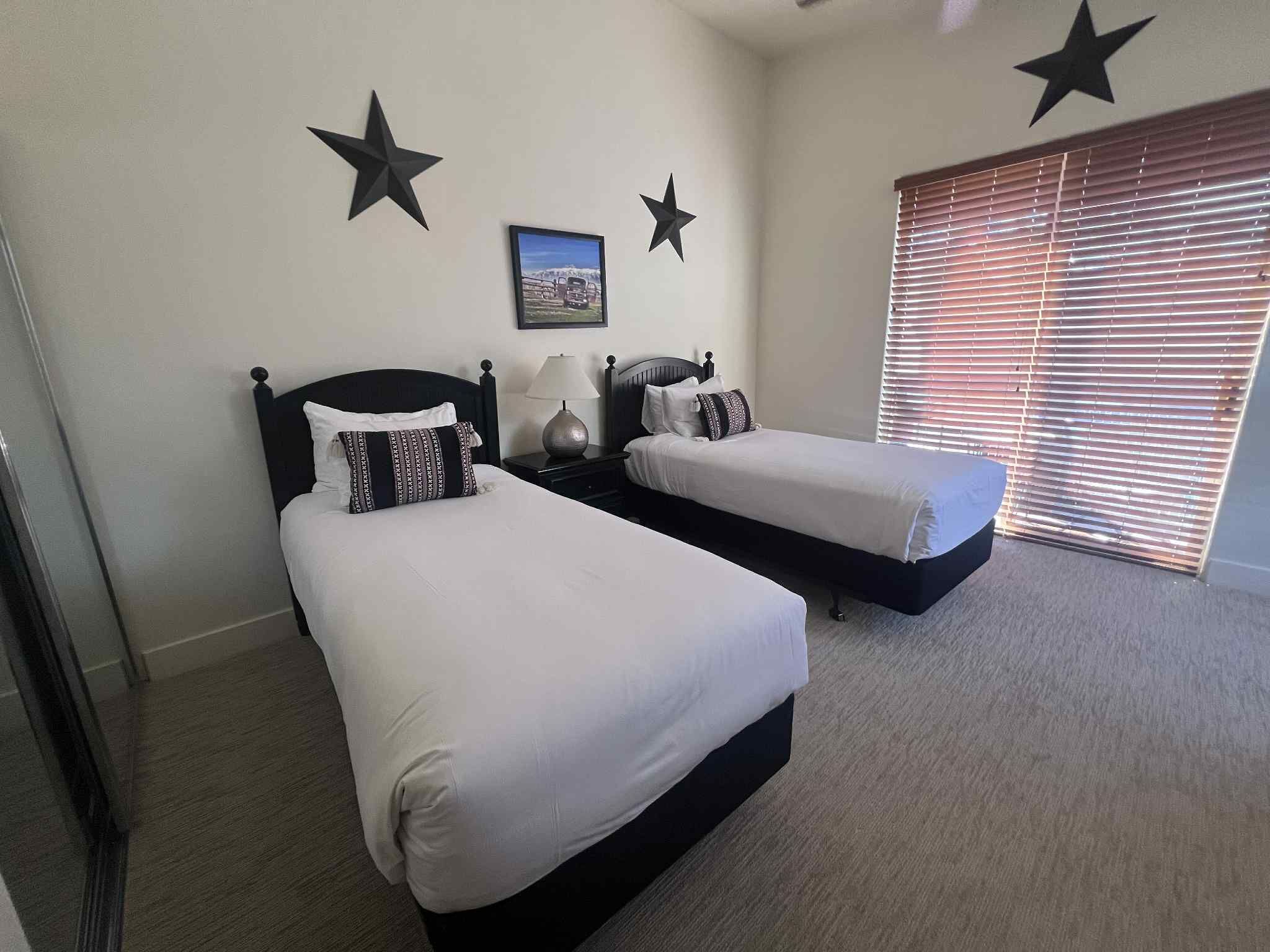 Quarto com duas camas, uma mesa de cabeceira, uma luminária e detalhes decorativos de estrelas na parede.