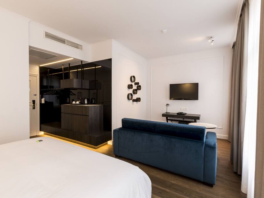 Quarto de hotel moderno com uma cama grande, um sofá azul, televisão de tela plana e um guarda-roupa embutido com espelho.