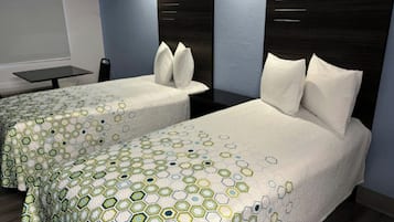 Duas camas de casal com colcha de padrão geométrico, cabeceira escura e uma pequena mesa com uma cadeira.