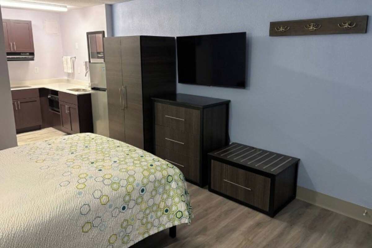 Quarto com cama, guarda-roupa, televisão e um pequeno armário.