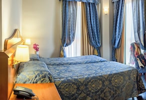 Quarto de hotel com duas camas, uma mesa de cabeceira com abajur, um telefone e uma luminária na parede.