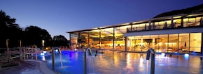 Um hotel moderno com uma piscina grande ao ar livre, fachada de vidro e interior bem iluminado.