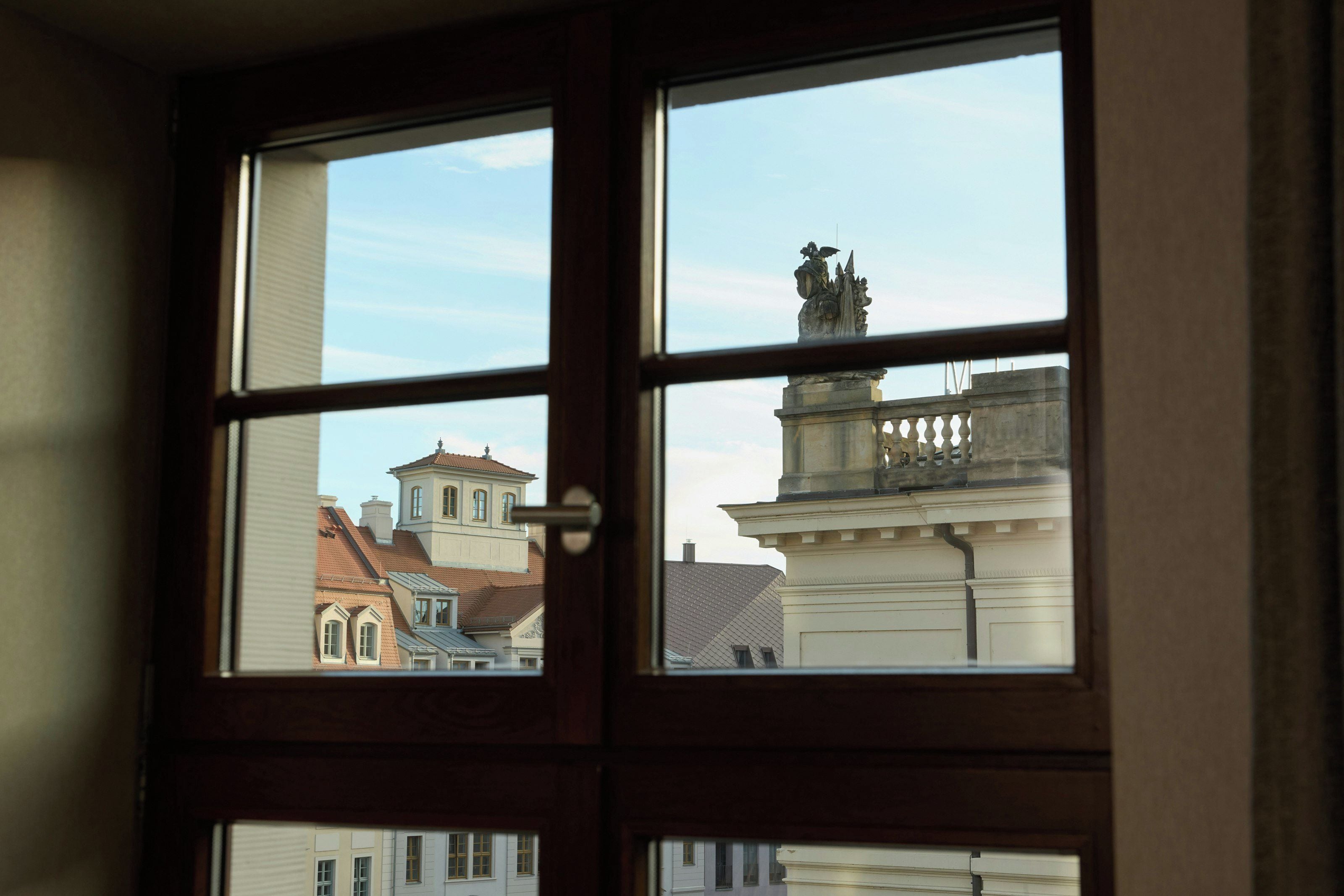 Janela com vista para um edifício e uma estátua no topo.