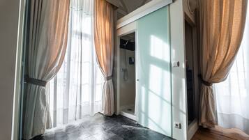 Quarto com área de chuveiro, porta de vidro e cortinas.