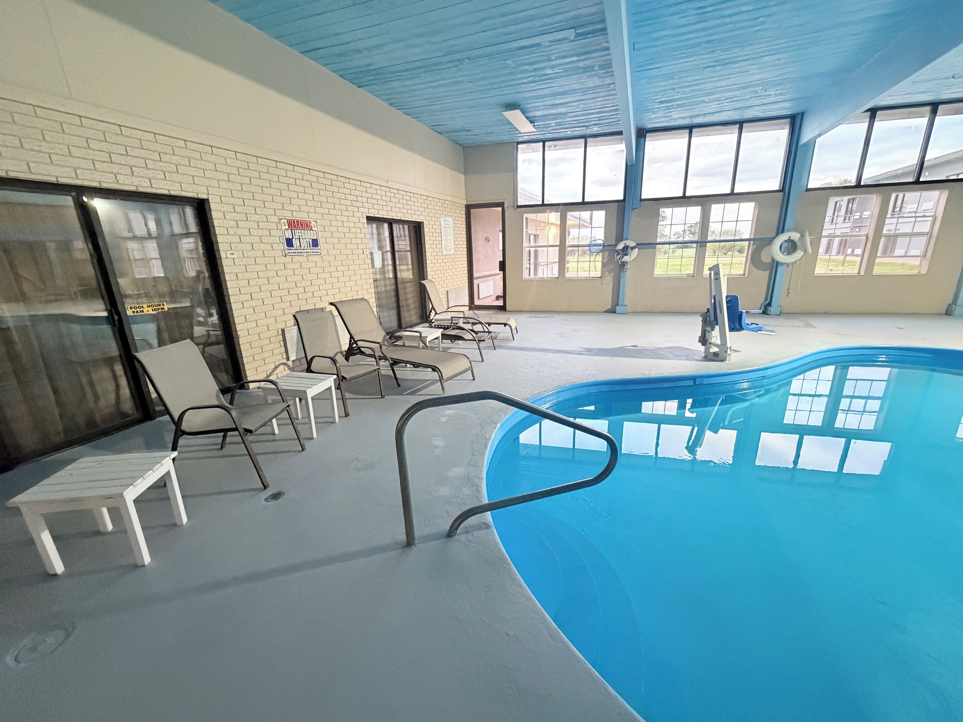 Piscina interna com espreguiçadeiras, placa de salva-vidas e janelas amplas.