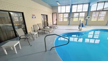 Piscina interna com espreguiçadeiras, placa de salva-vidas e janelas amplas.