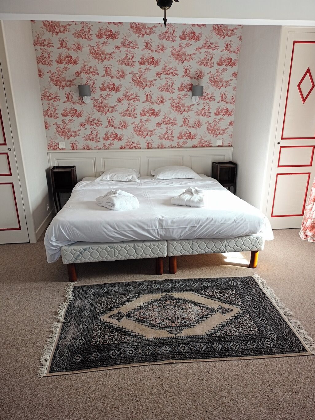 Cama bem arrumada com lençóis brancos e um tapete estampado em frente.