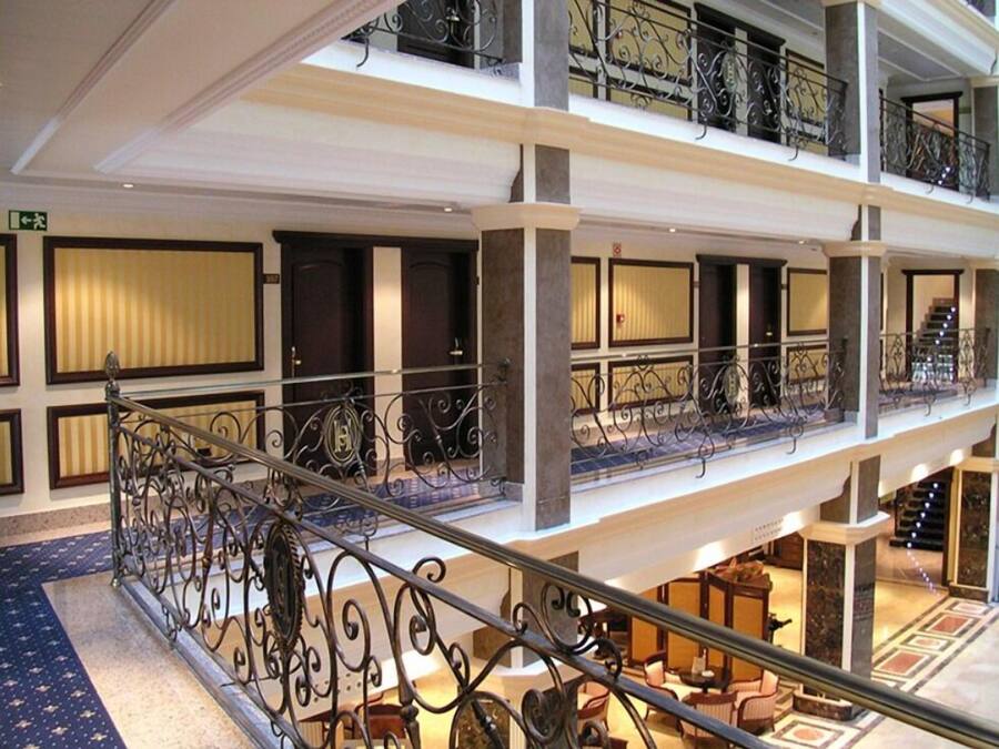 Interior de um hotel com vários níveis, uma escadaria central, várias varandas e uma área de recepção com assentos.