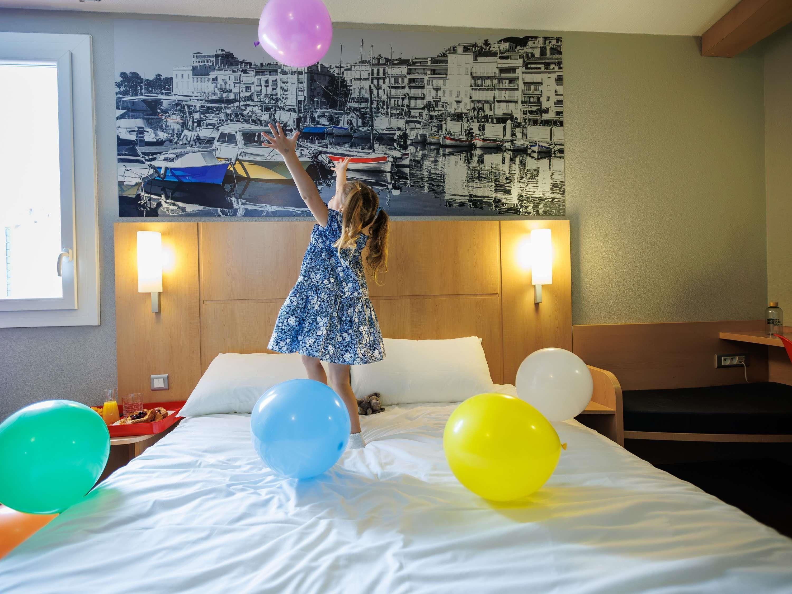 Quarto de hotel com cama, quadro pendurado na parede mostrando um porto e mesa de cabeceira com uma garrafa.