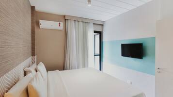 Quarto de hotel com cama, televisão de tela plana na parede, janela com cortinas e aparelho de ar condicionado.