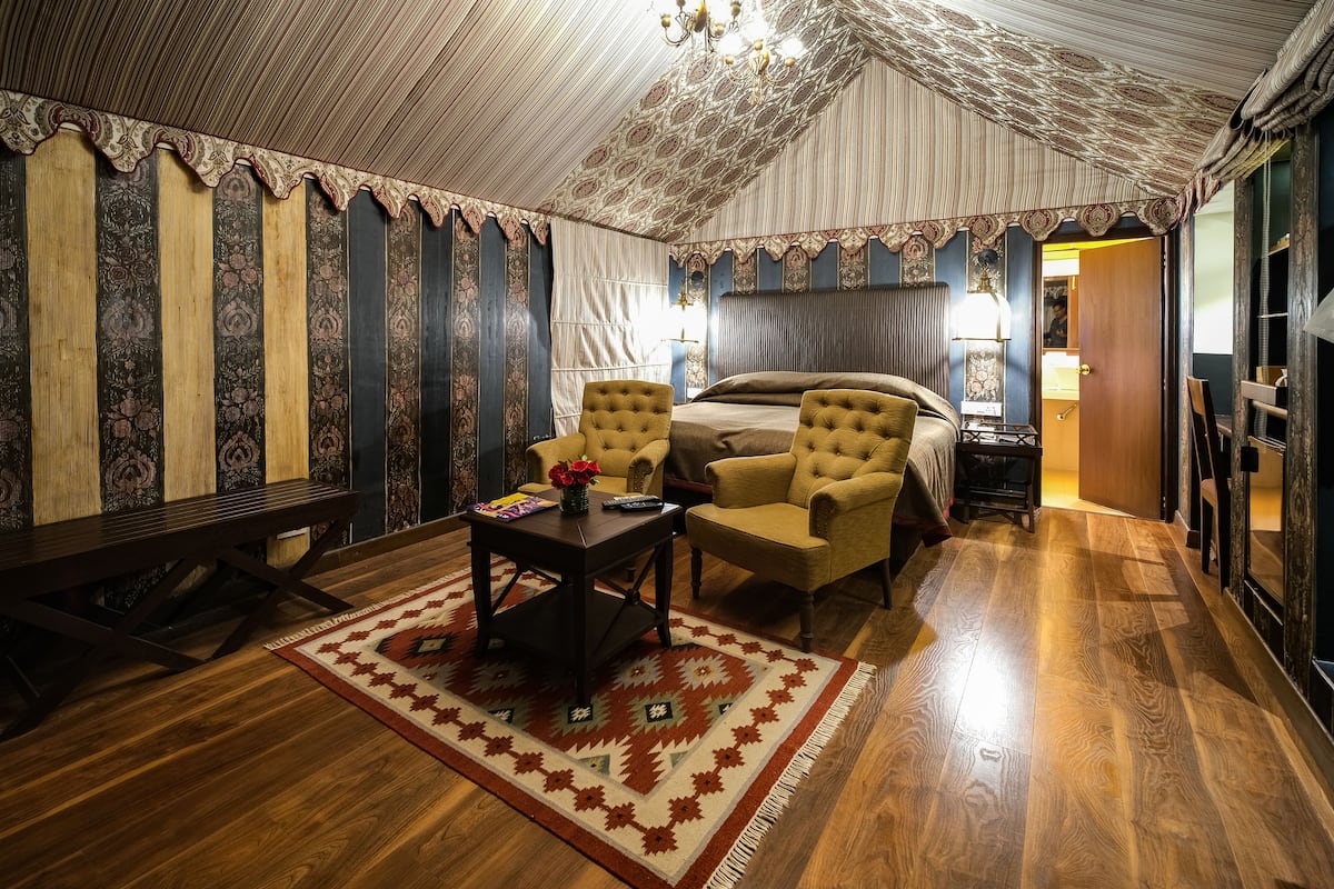 Quarto com cama, duas poltronas, uma mesinha e uma luminária.