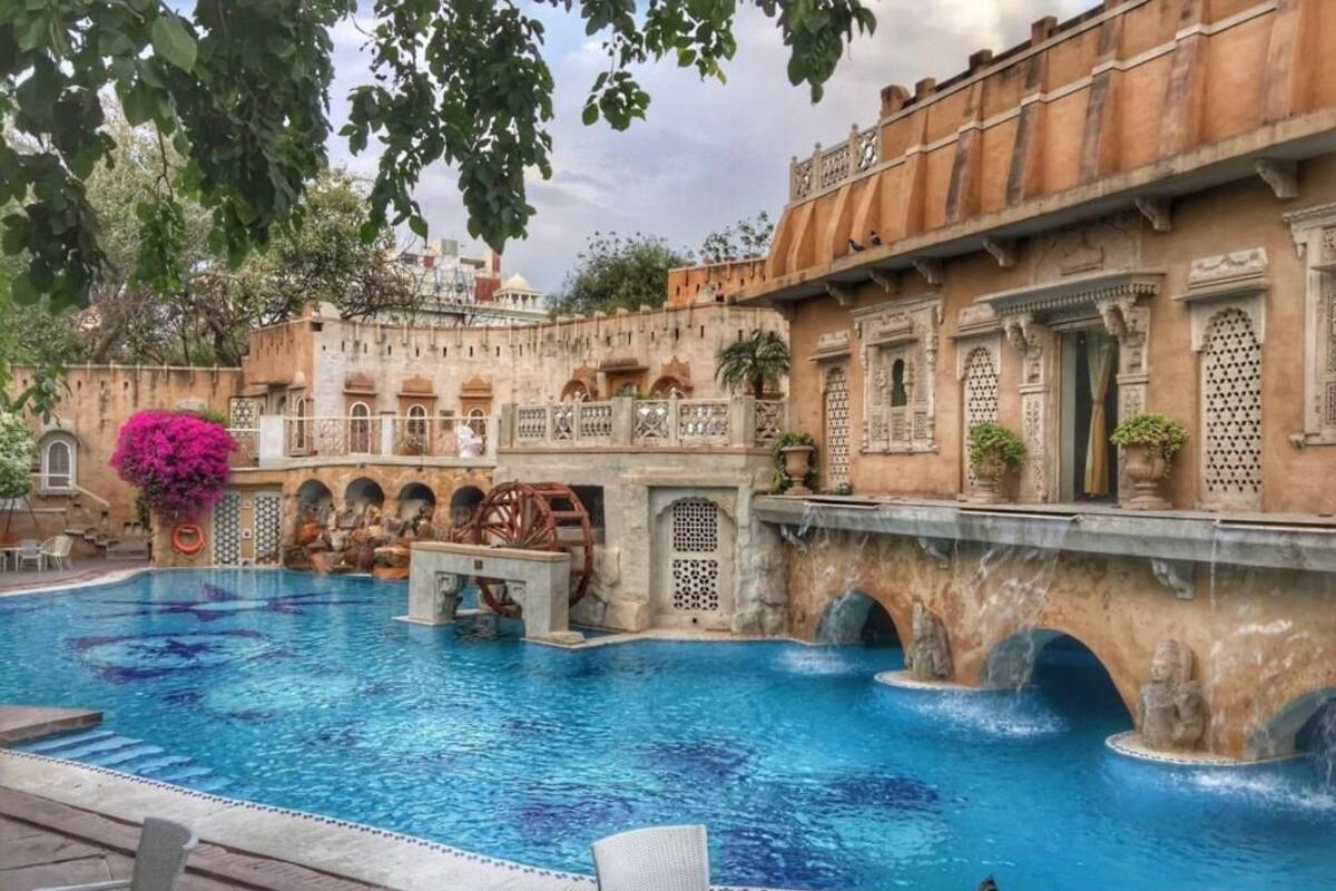 Piscina com uma ponte de pedra, rodeada por arquitetura tradicional.