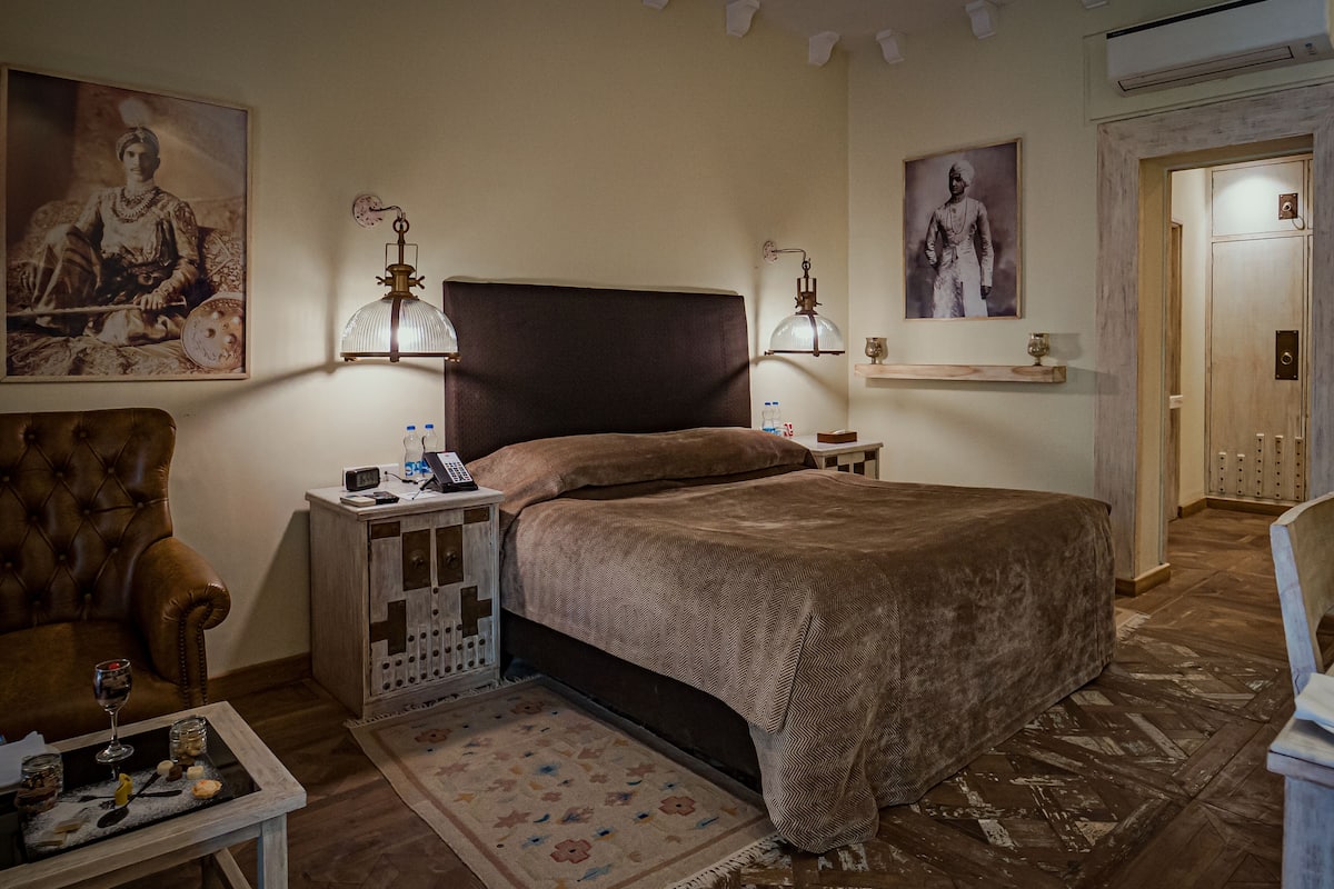 Quarto com uma cama grande, uma poltrona de couro, uma mesa pequena com um copo e duas luminárias na parede.