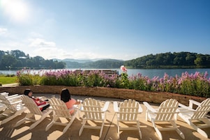 Um alpendre à beira do lago com cadeiras Adirondack e vista para o lago e as colinas.