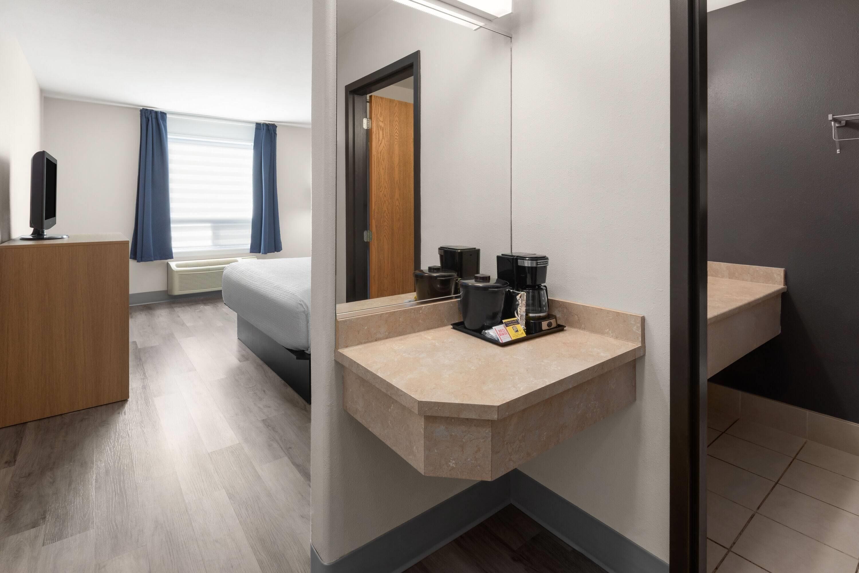 Quarto de hotel com cama, escrivaninha, cafeteira e espelho.