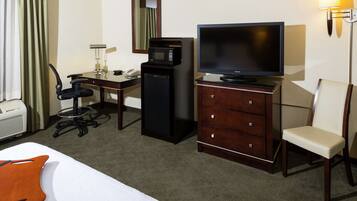 Quarto de hotel com cama, escrivaninha com computador, televisão, micro-ondas, cadeira e abajur.