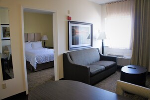 Quarto de hotel com cama, sofá, mesa pequena e uma cadeira.