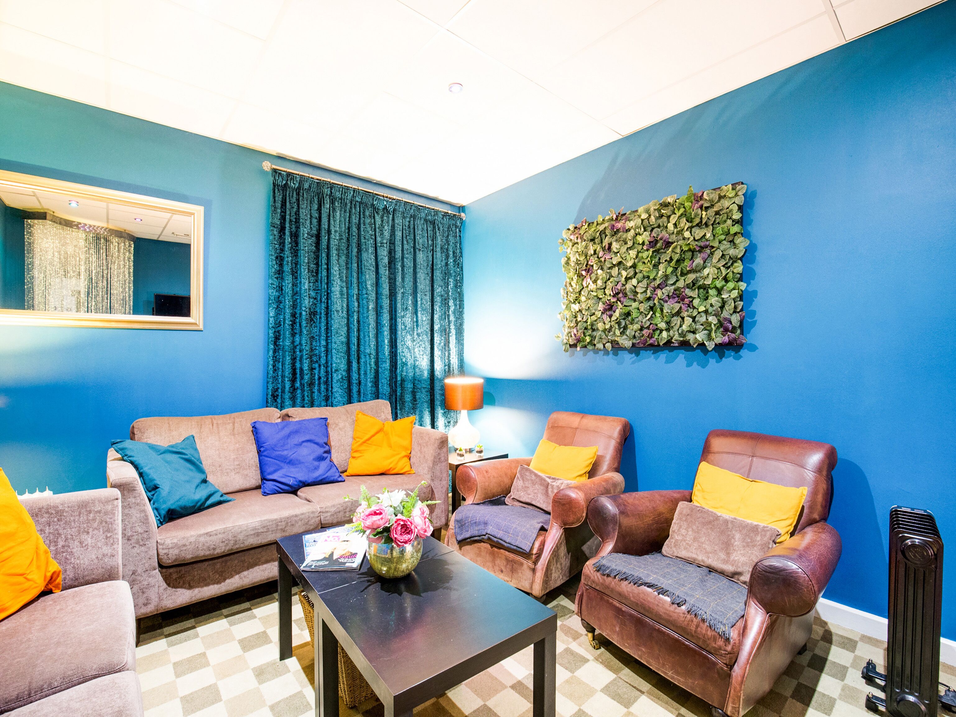 Uma sala de estar com parede azul, espelho, sofá, poltrona, mesa e uma planta decorativa.