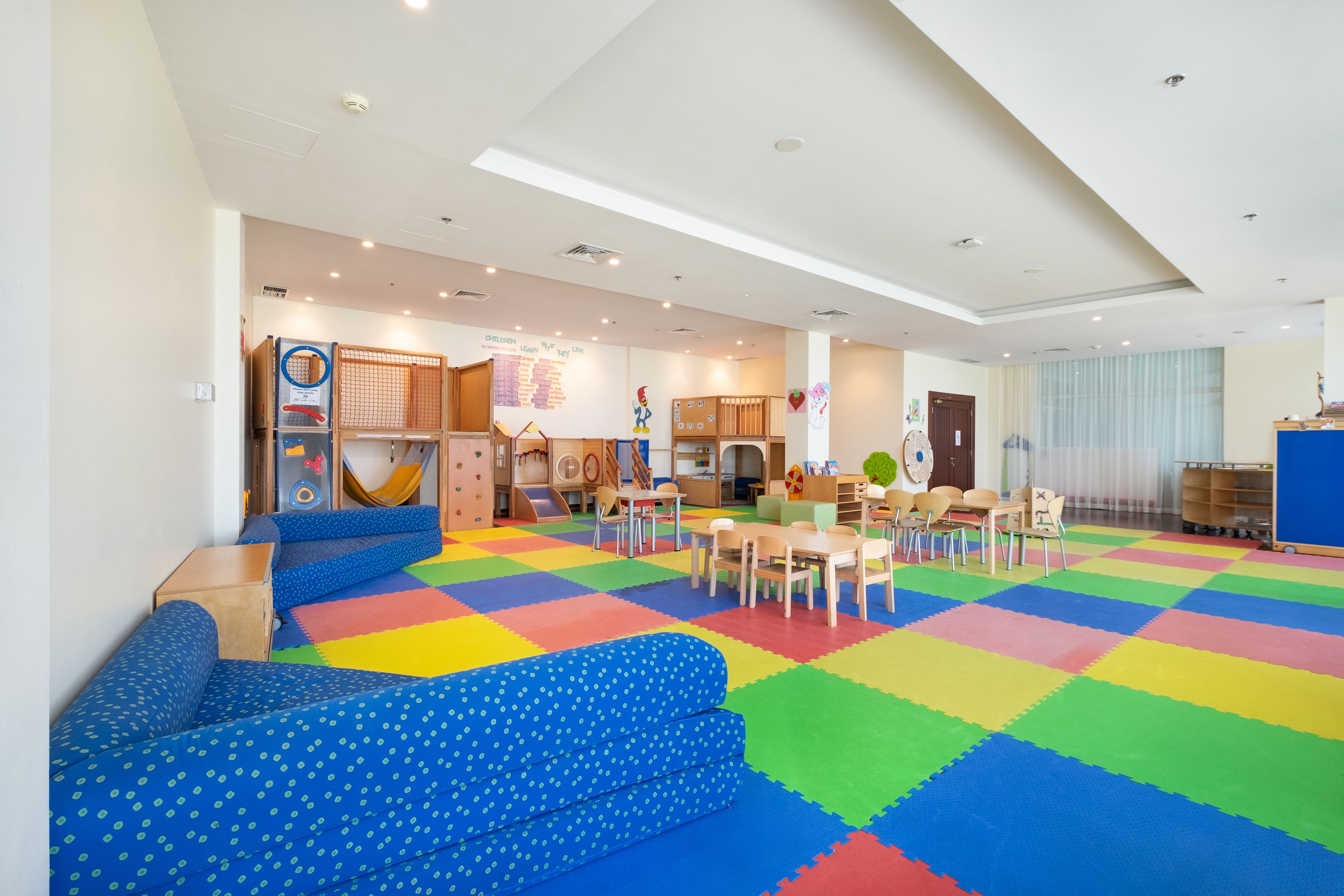 Espaço infantil com tapetes de espuma coloridos, um sofá azul e uma mesa de brincar.