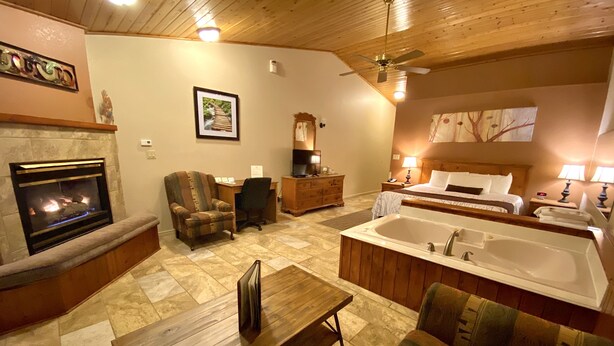 Um quarto aconchegante com lareira, uma banheira grande, uma poltrona confortável, uma mesa de madeira e uma cama com mesa de cabeceira.