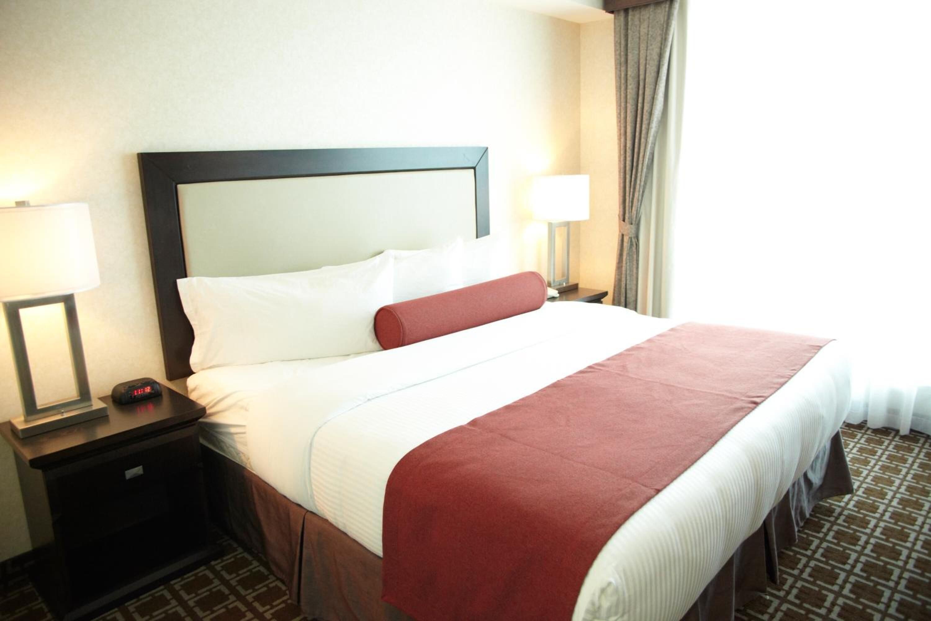 Quarto de hotel com cama grande, duas mesas de cabeceira e uma luminária.