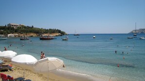 Uma praia com águas cristalinas, vários barcos e guarda-sóis.