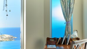 Quarto com vista para o mar, uma escrivaninha de madeira com uma luminária e uma cadeira.