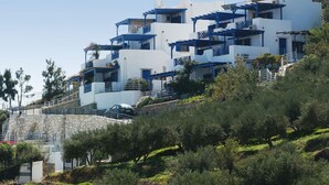 Um edifício com vários andares e varandas, cercado por vegetação e um muro de pedra.