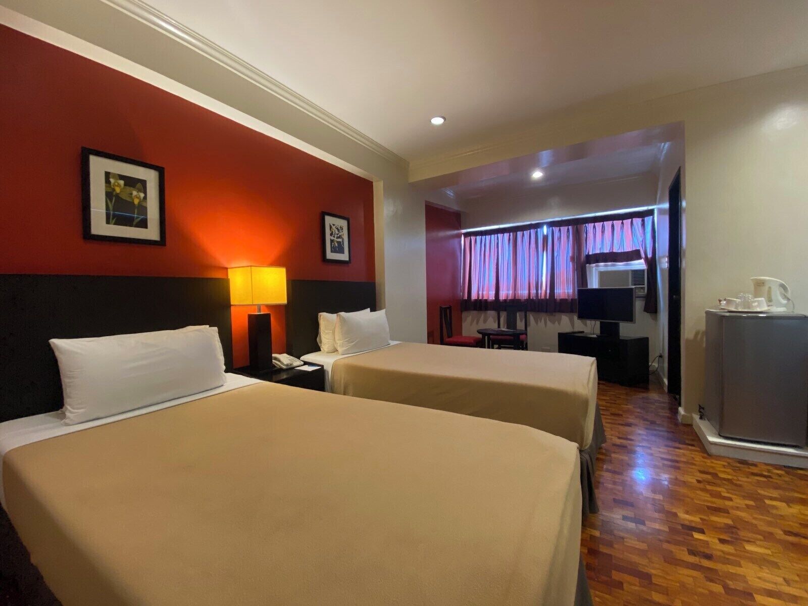 Quarto de hotel com duas camas, uma escrivaninha, uma cadeira, televisão e máquina de café.