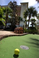 Um buraco de mini golfe com uma bola de golfe amarela e uma tampa de bueiro com a inscrição 'Stanford Golf'.