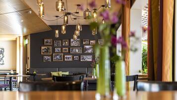 Interior de restaurante com luminárias pendentes, parede com fotografias emolduradas e mesa com cadeiras.