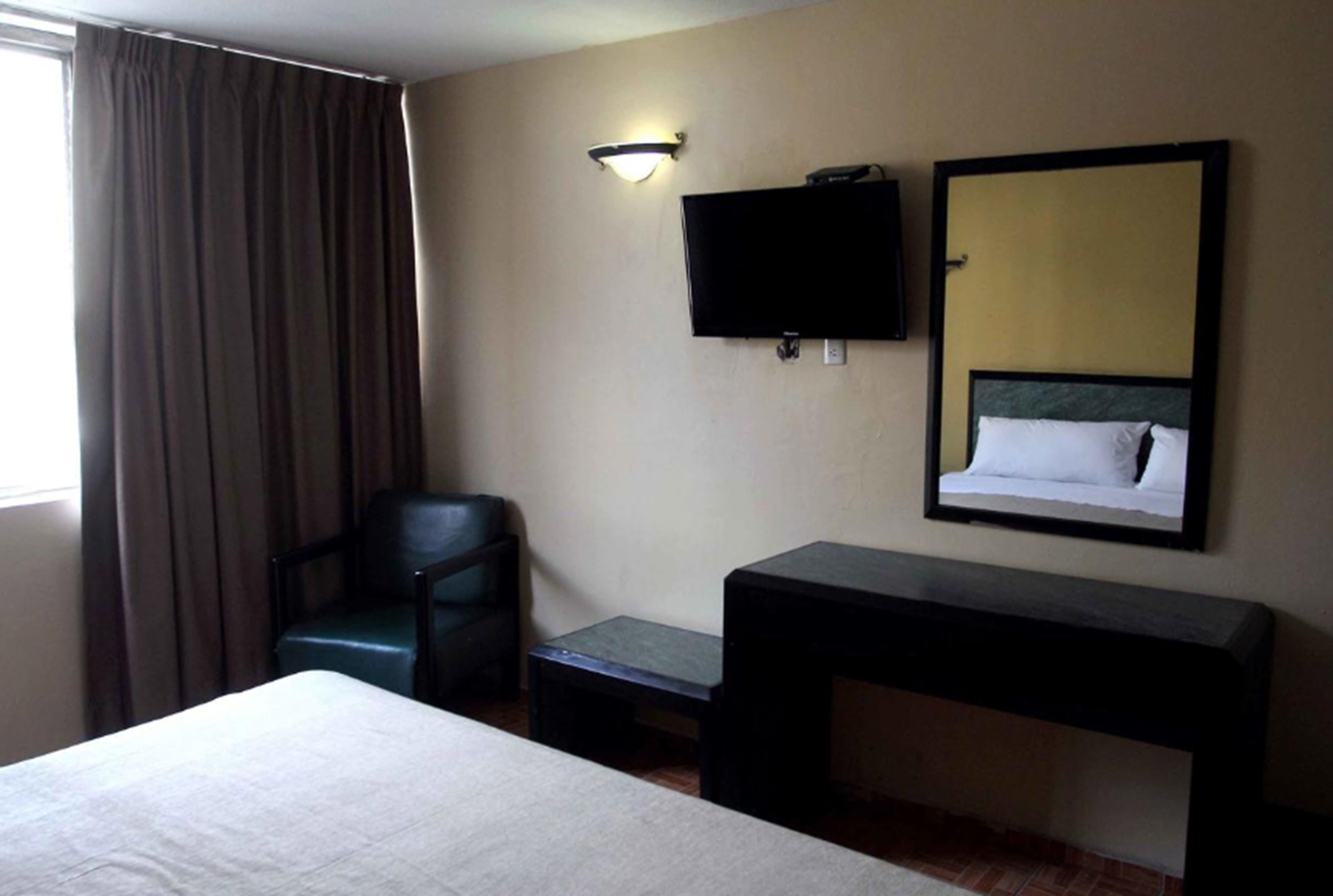 Quarto de hotel com cama, escrivaninha, cadeira, televisão e espelho.