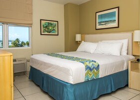 Quarto de hotel com cama, janela com vista, quadro pendurado na parede e mesa de cabeceira.