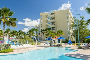 Um hotel com piscina, palmeiras e um céu azul límpido.