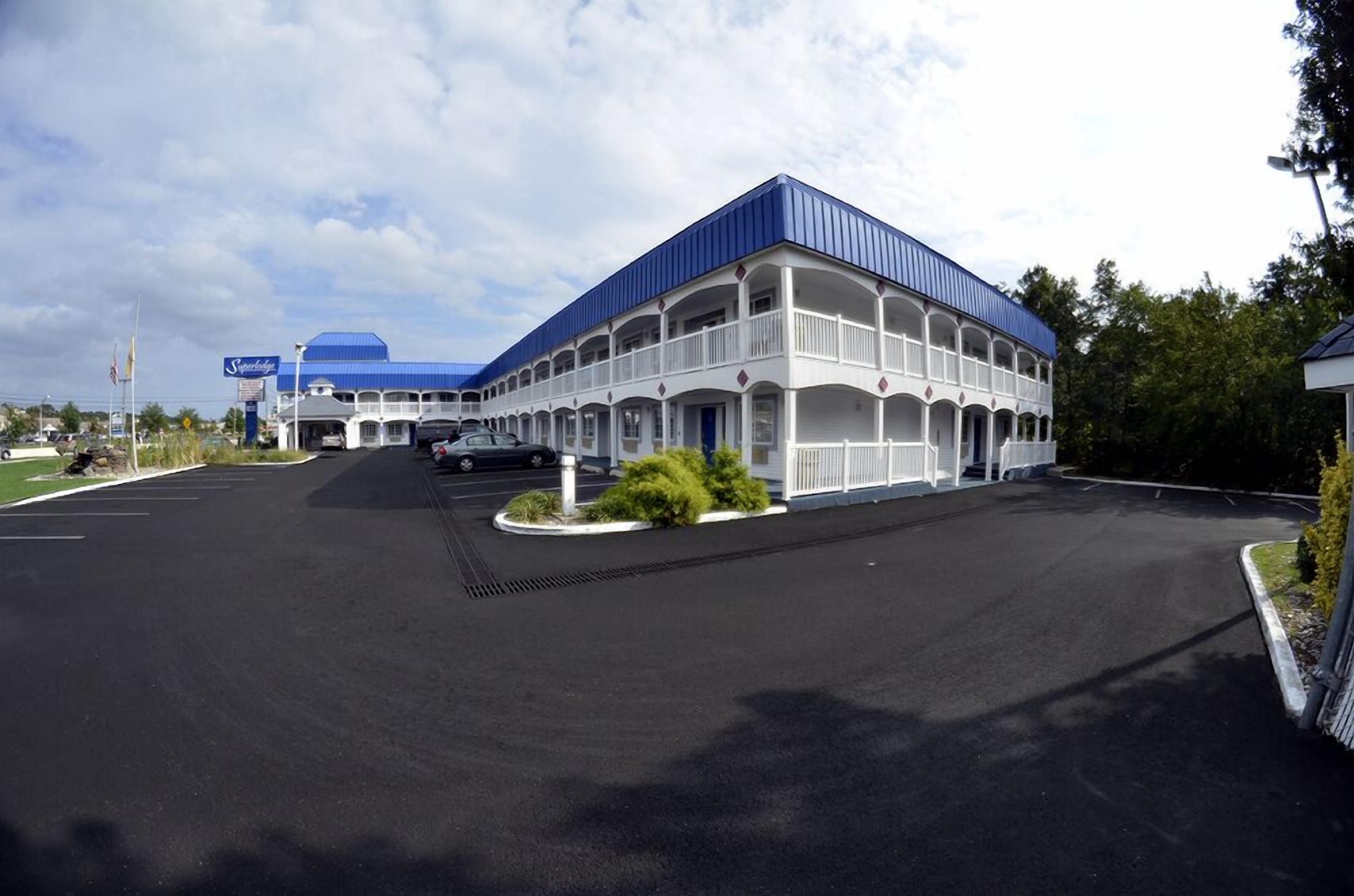Um motel com telhado azul e fachada branca, apresentando um pátio central e várias varandas.
