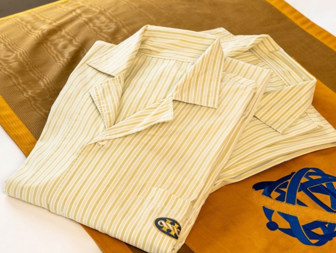 Uma camisa listrada, bem dobrada, com um logotipo no bolso, apoiada em uma superfície de madeira.