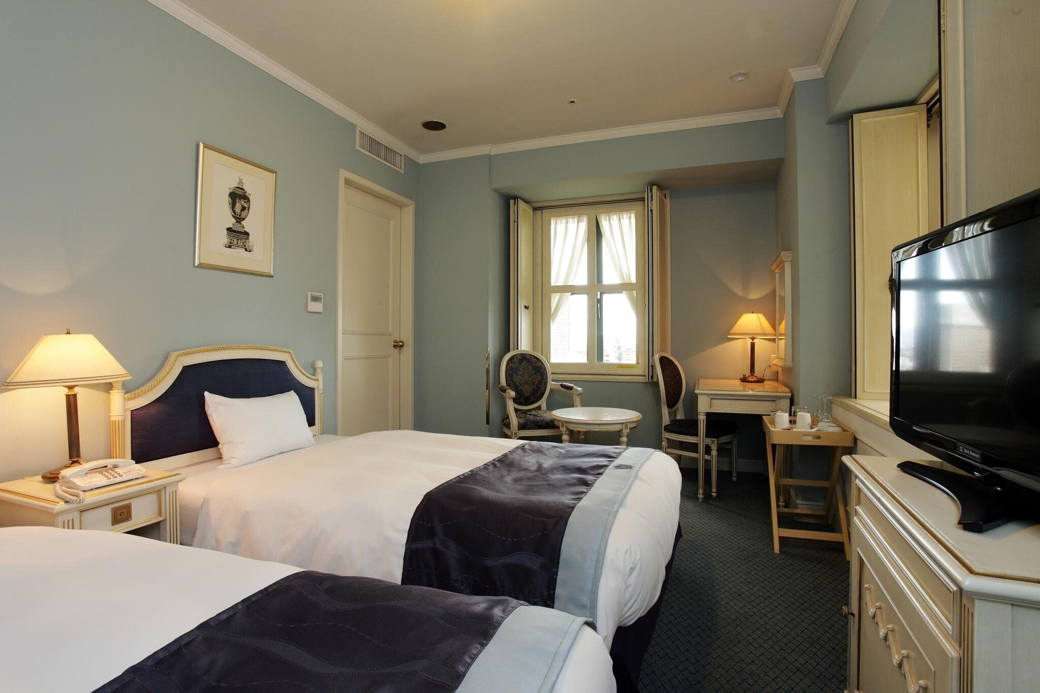 Quarto de hotel com duas camas, uma escrivaninha, televisão e uma cadeira.