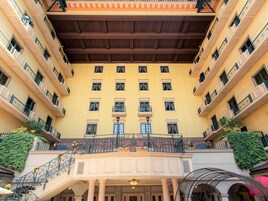 Um hotel com vários andares, fachada amarela, varandas com grades e uma escadaria central.