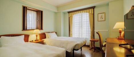 Quarto de hotel com duas camas, uma escrivaninha, uma cadeira e uma luminária.