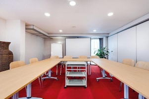 Uma sala de conferências com uma mesa comprida, cadeiras, uma tela de projetor e um quadro branco.