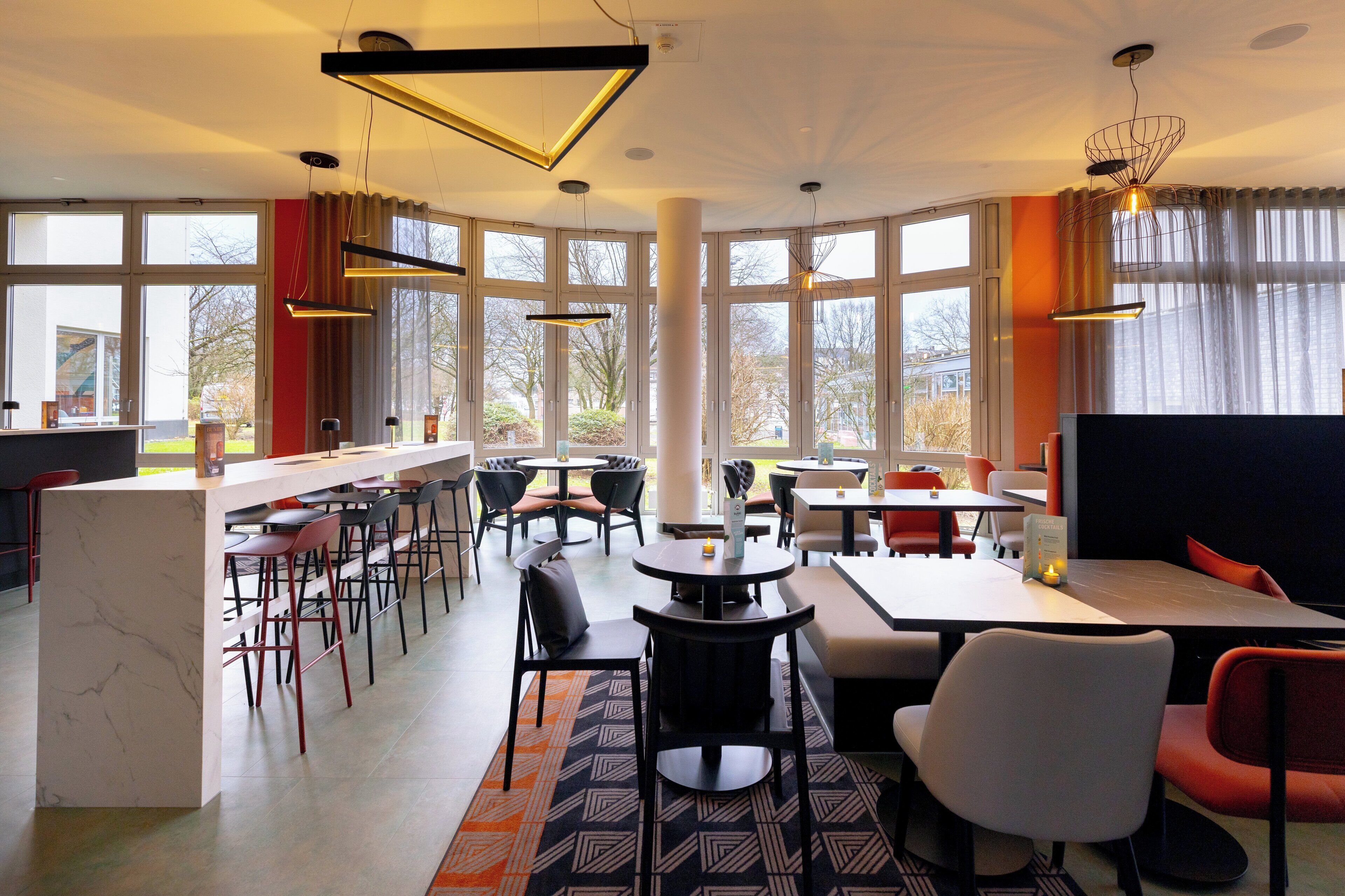 Uma sala de jantar moderna com um balcão de mármore, várias mesas e cadeiras, e grandes janelas com vista para o exterior.