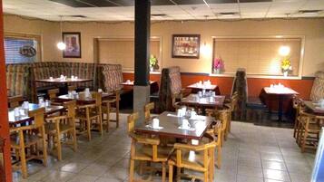 Um restaurante com cabines e mesas, cadeiras de madeira, piso de azulejos e quadros nas paredes.
