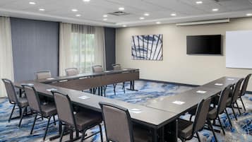 Uma sala de conferências com uma mesa comprida, cadeiras, uma tela de projetor e um quadro branco.