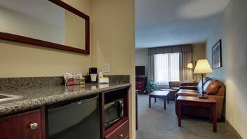 Quarto de hotel com cozinha equipada, incluindo lava-louças, micro-ondas e bancada de granito. Possui sala de estar com sofá, mesa e luminária.