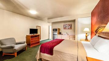 Quarto de hotel com cama, poltrona, televisão, escrivaninha e cozinha compacta.