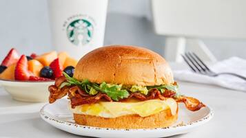 Um sanduíche de café da manhã em um prato, com uma xícara da Starbucks ao fundo.