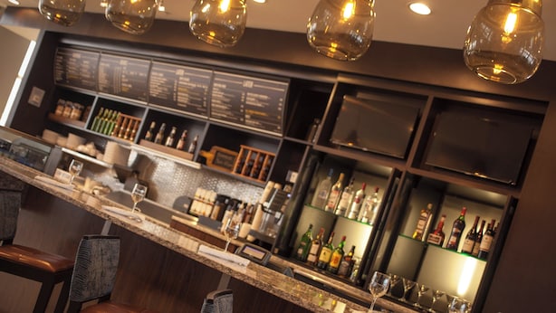 Uma área de bar com bancada de mármore, banquetas e prateleiras cheias de garrafas.