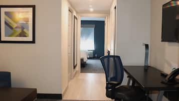 Quarto de hotel com escrivaninha, cadeira e cama. Há um quadro na parede e uma televisão também.