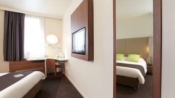 Quarto de hotel com duas camas de solteiro, uma escrivaninha, uma cadeira, uma televisão e um espelho.